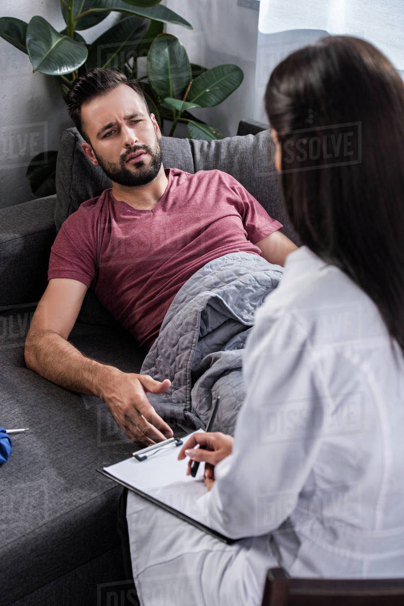 Rear view of female doctor with clipboard sitting near suffering ...