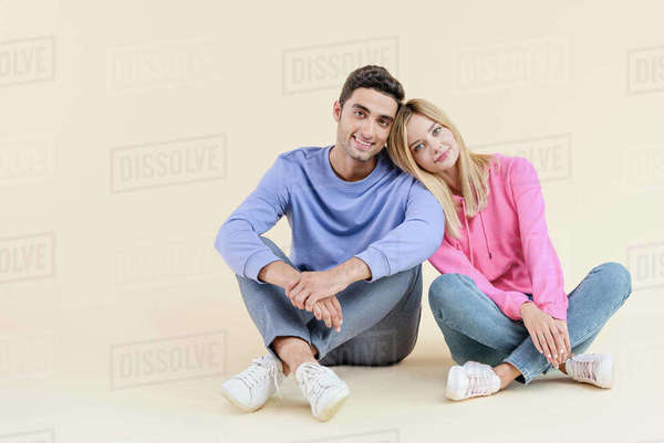 Beautiful happy young couple sitting together and smiling at camera ...