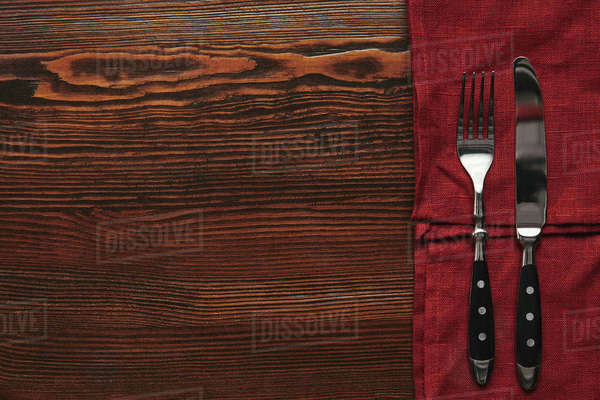 Top view of fork and knife on dark red tablecloth on wooden table ...