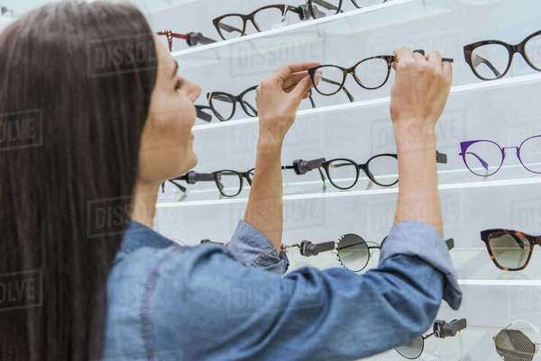 Side view of attractive young woman taking eyeglasses from shelves in ...