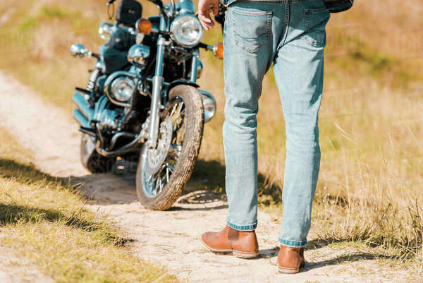 Cropped view of man walking along trail near retro motorbike - Royalty ...
