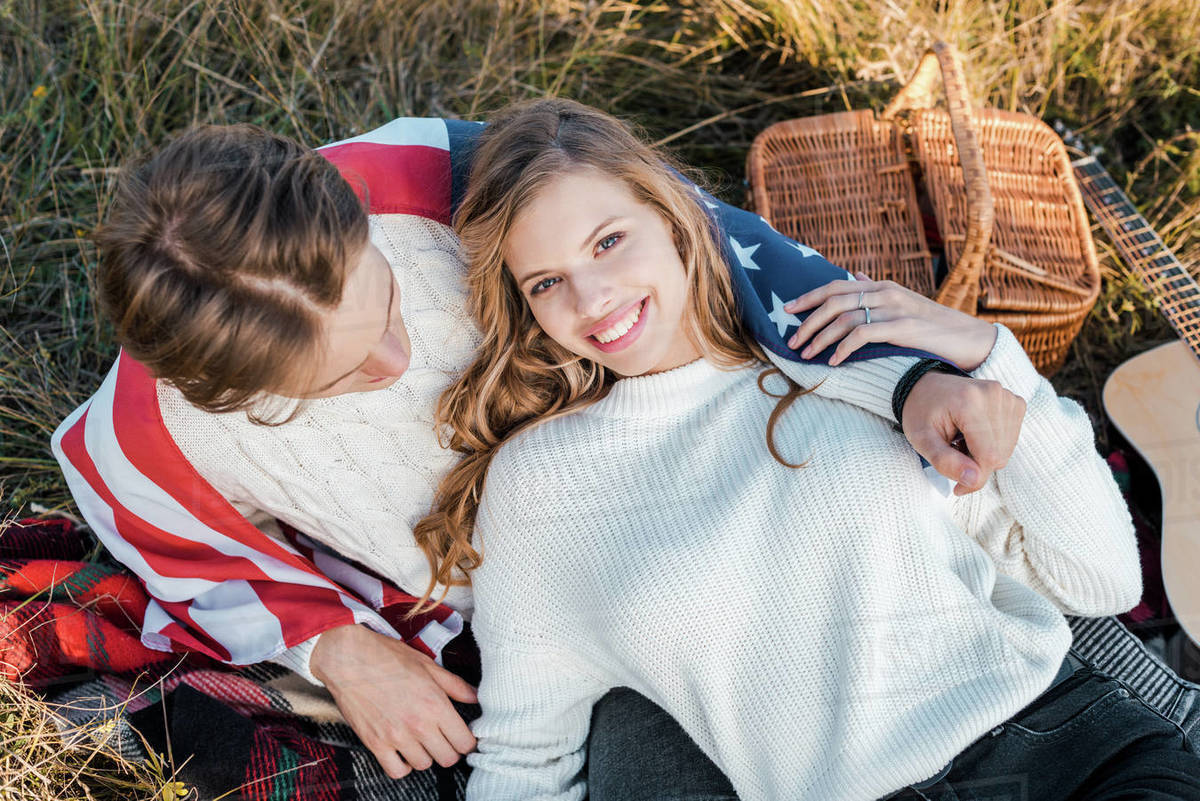 Attractive couple with American flag relaxing on grass, independence ...