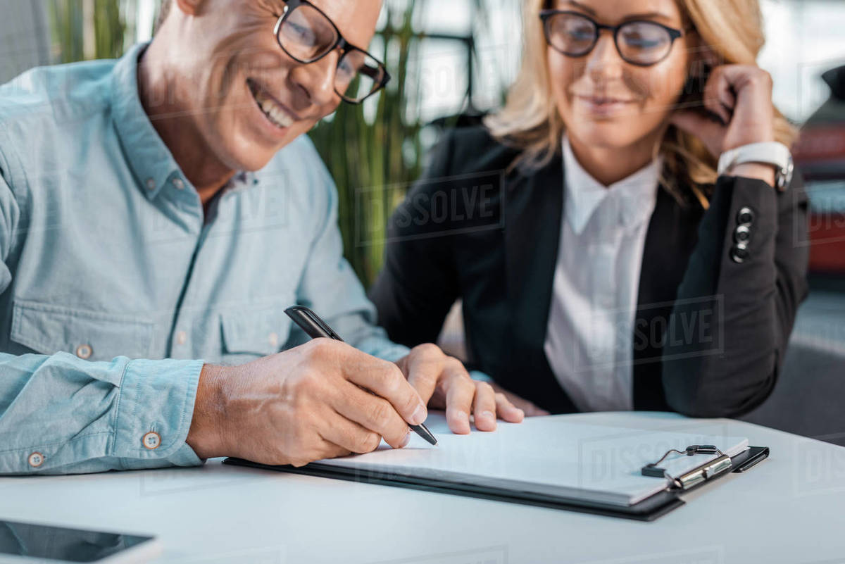 Smiling adult customer signing contract with female car dealer at ...