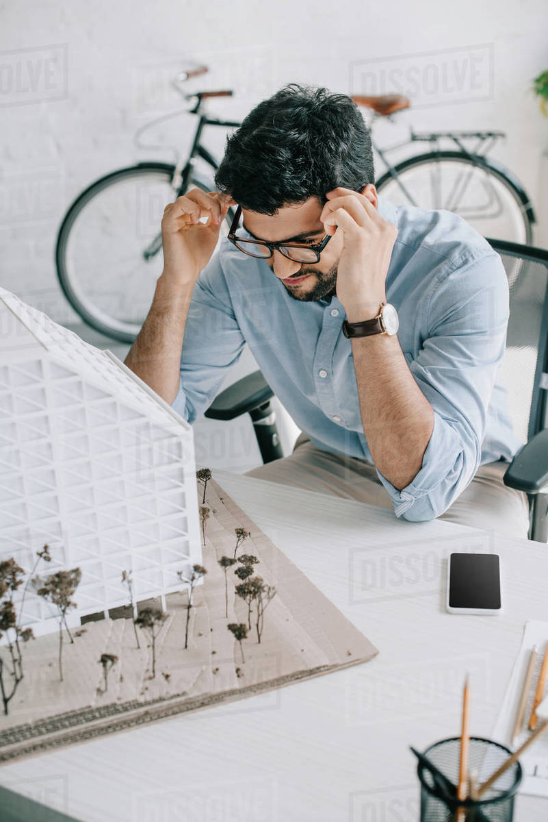 Handsome architect touching head and looking at architecture model in ...