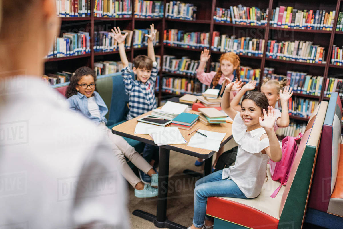 adorable little kids raising hands in library - Stock Photo - Dissolve