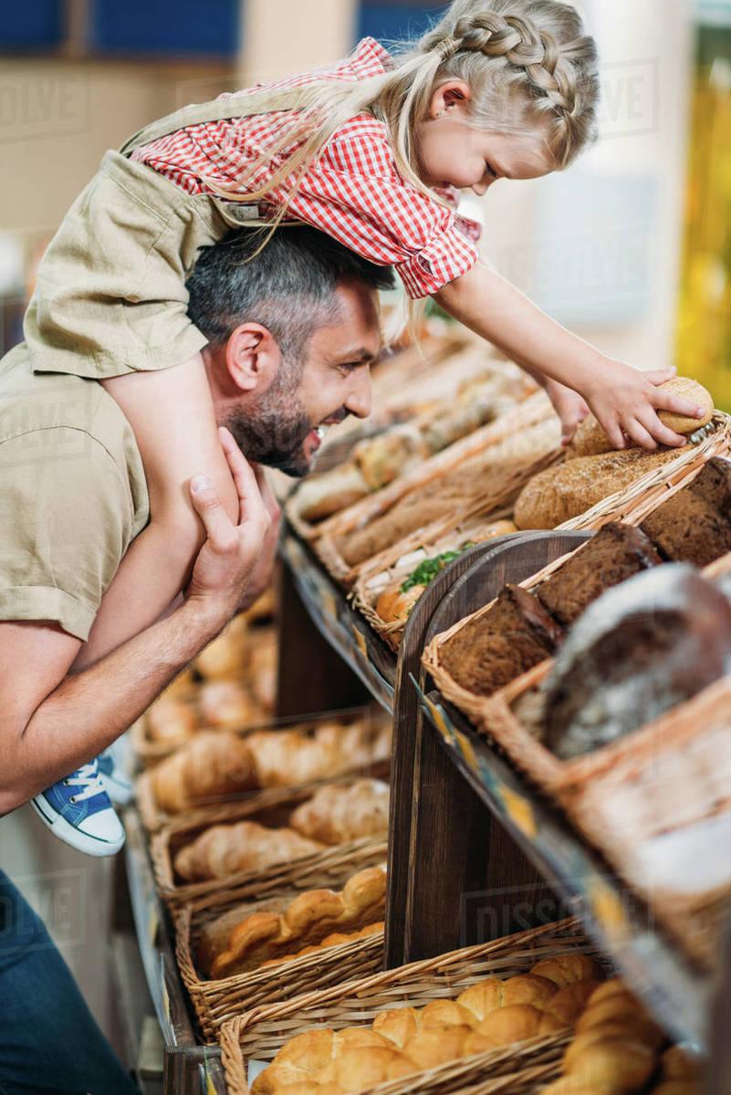 side view of happy father and daughter buying bread in supermarket ...