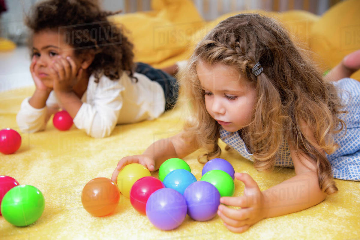 Adorable multiethnic kids playing on yellow carpet with colored balls ...
