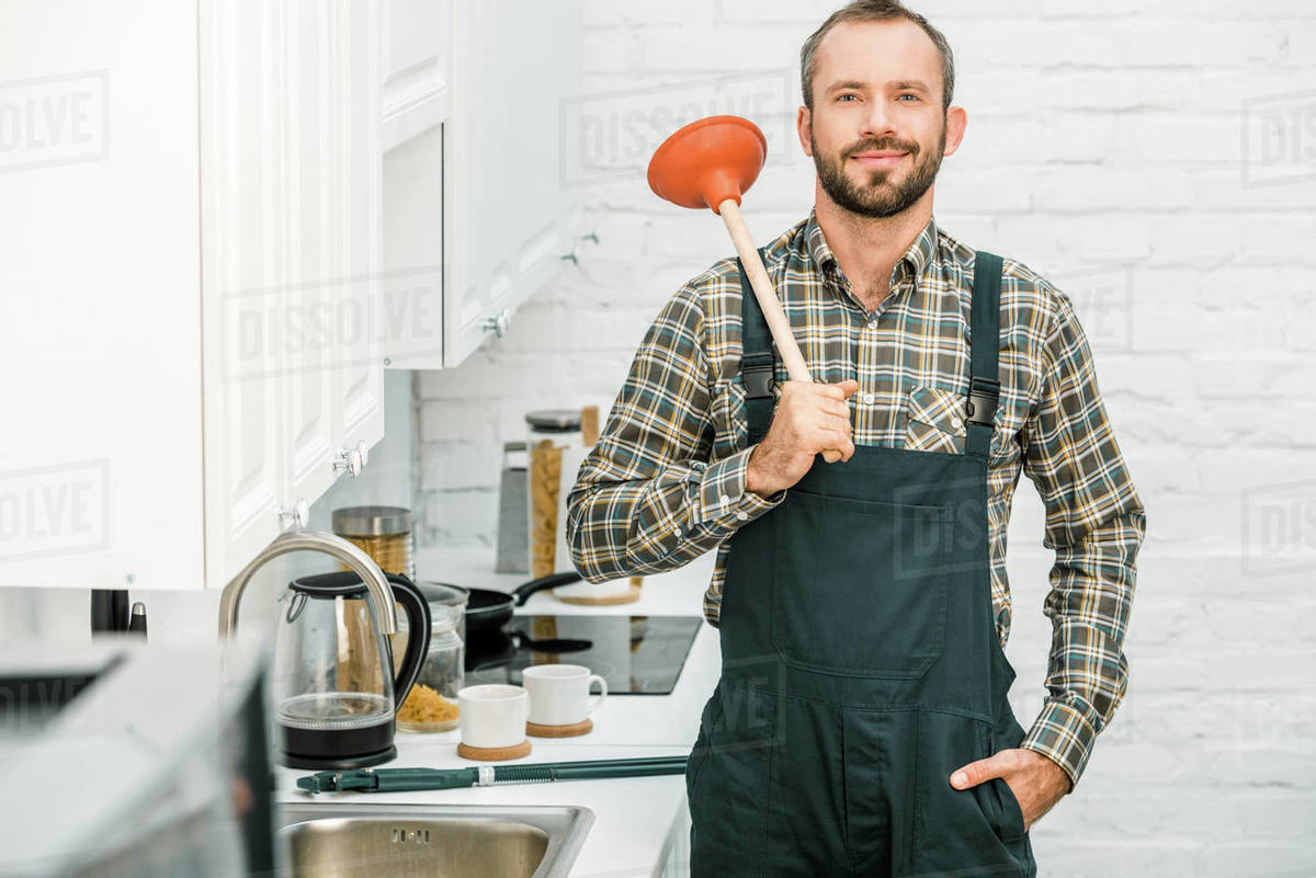 Cheerful handsome plumber holding plunger on shoulder and looking at ...