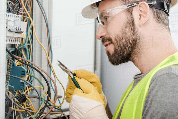 Side view of handsome electrician holding pliers and looking at ...