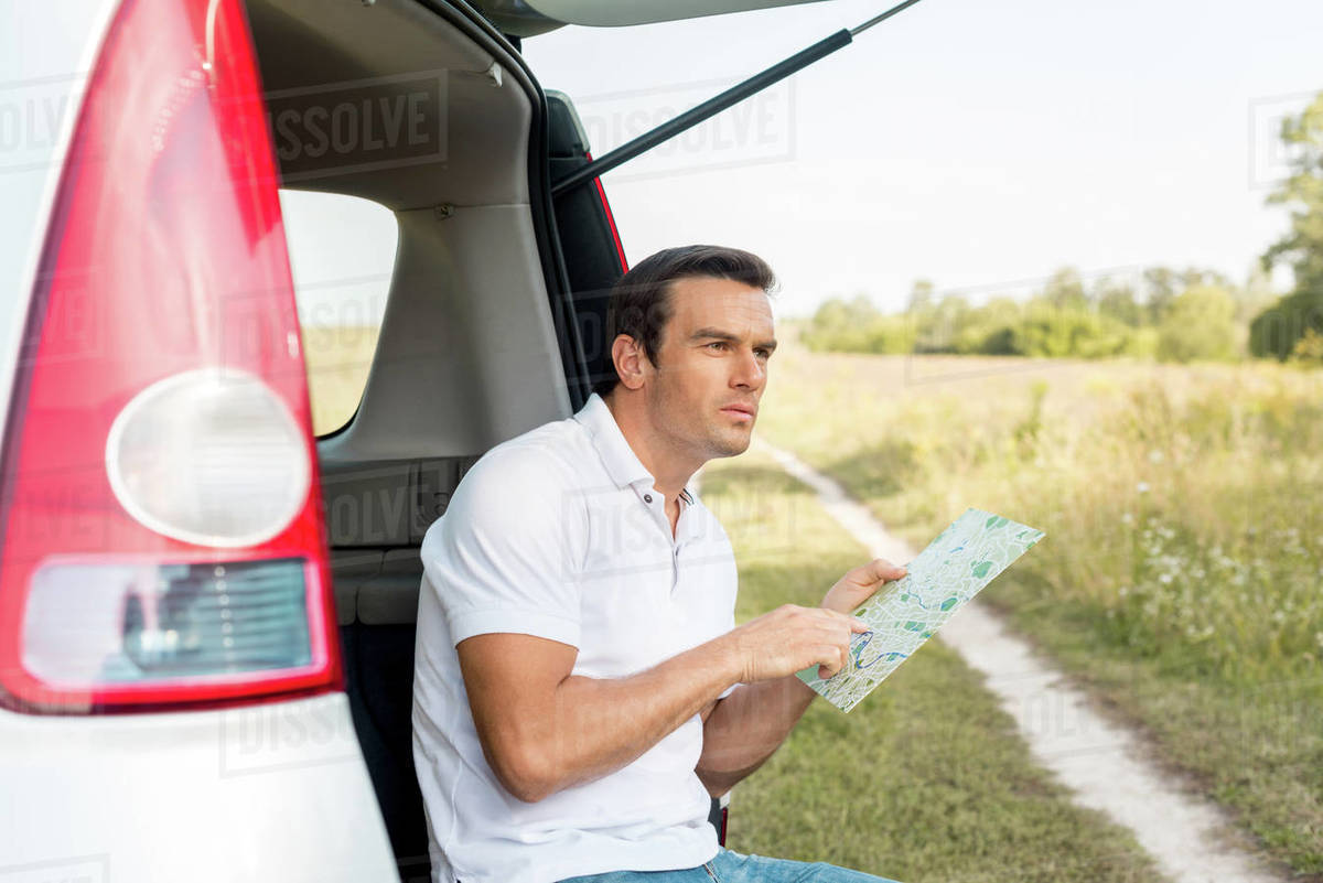lost man sitting in car trunk and navigating with map in field ...
