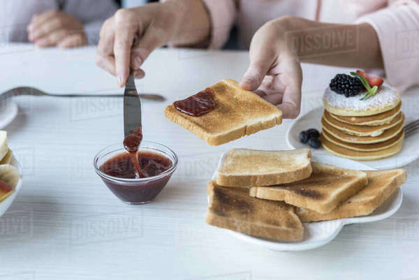 Cropped shot of mother preparing toast with jam for her little child at ...