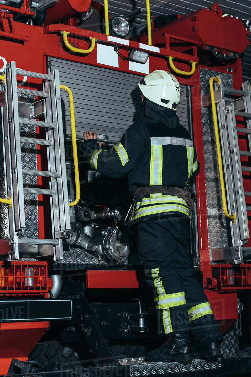 back view of firefighter in fireproof uniform and helmet closing truck ...