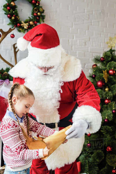 Santa Claus looking at little child with wish list - Stock Photo - Dissolve