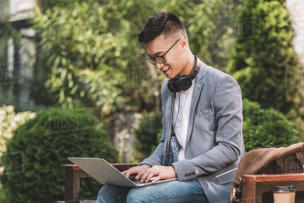 Stylish Asian freelancer in gray jacket working on laptop while sitting ...