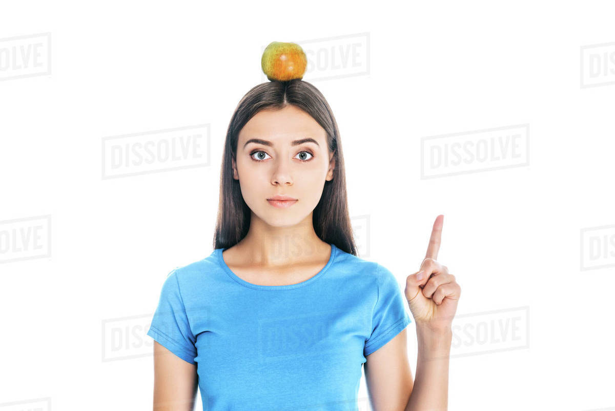 Portrait of young woman with fresh apple on head pointing up isolated ...