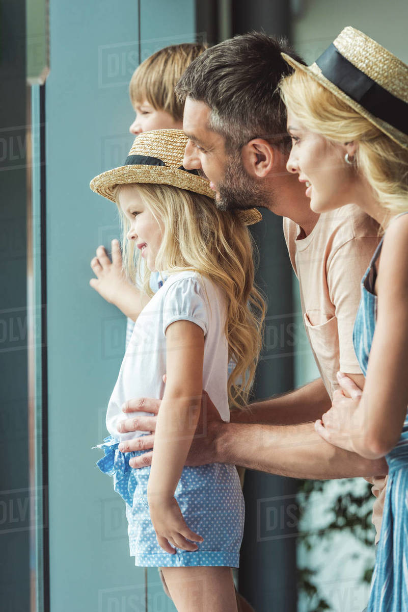 Side view of happy family looking out window in airport - Royalty-free ...
