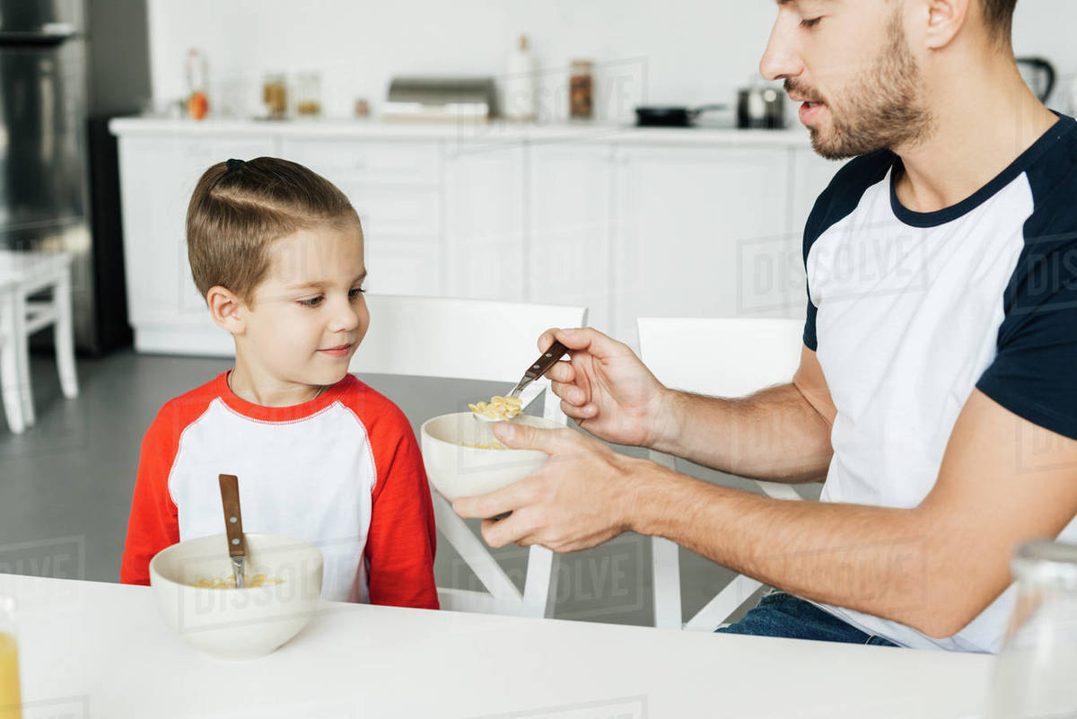 Father feeding son while having breakfast together in kitchen - Royalty ...