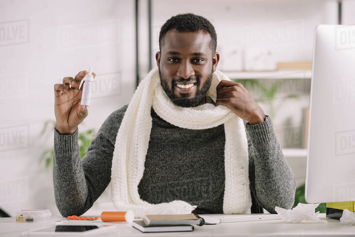Cold smiling African American businessman in warm scarf with nose spray ...