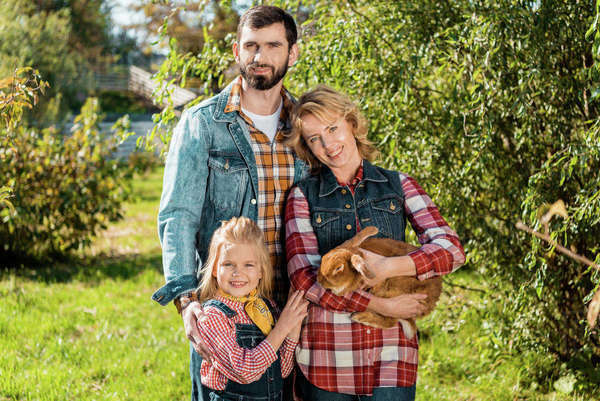 Happy farmer family with little daughter and brown rabbit outdoors ...