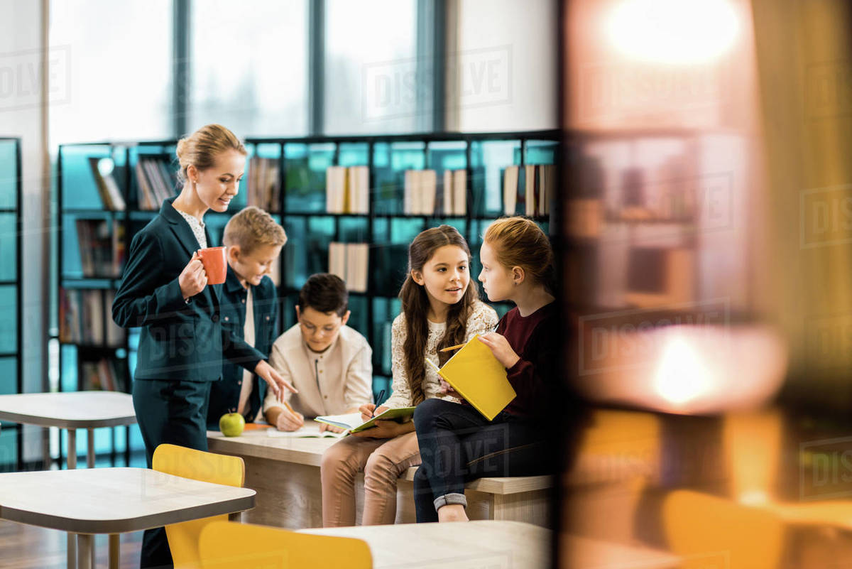 Selective focus of schoolchildren and librarian talking together in ...