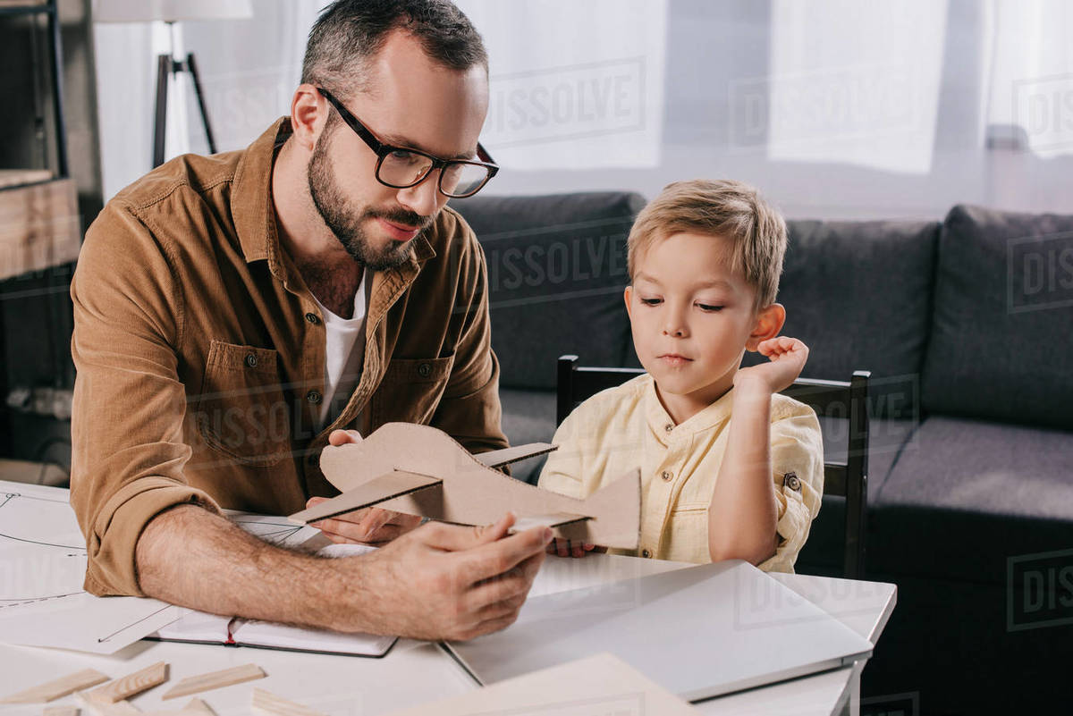 Father in eyeglasses and cute little son modeling plane together at ...