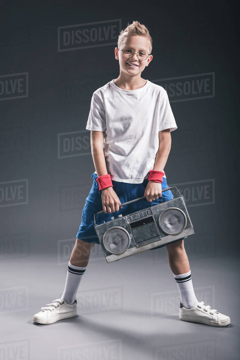 Stylish smiling boy in eyeglasses with boombox posing on grey backdrop ...