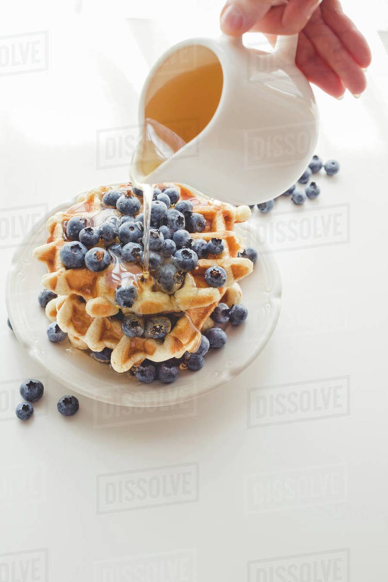 Cropped shot of woman pouring syrup from saucer on tasty waffles ...