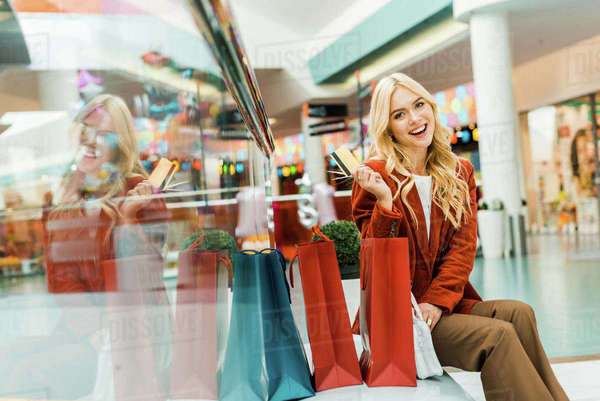 Excited woman holding credit card and sitting with shopping bags in ...