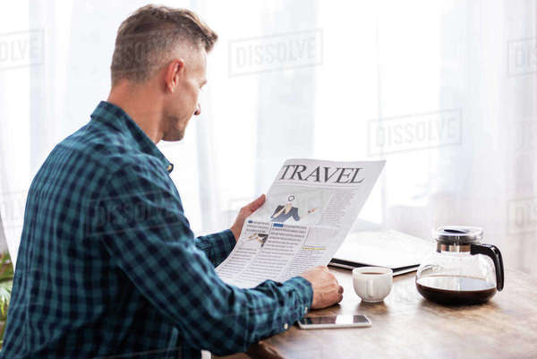 Rear view of man sitting at table and reading travel newspaper in ...