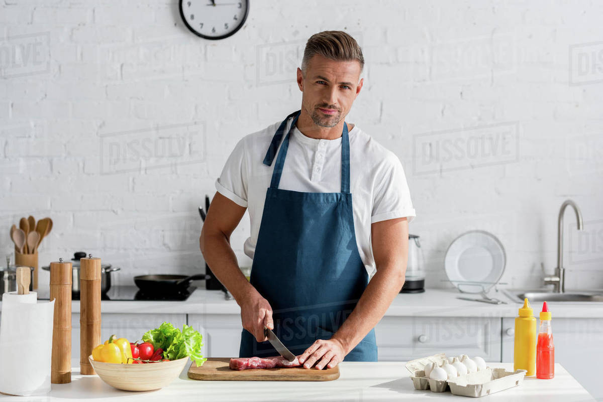 Handsome man cutting pork meat on the kitchen - Stock Photo - Dissolve