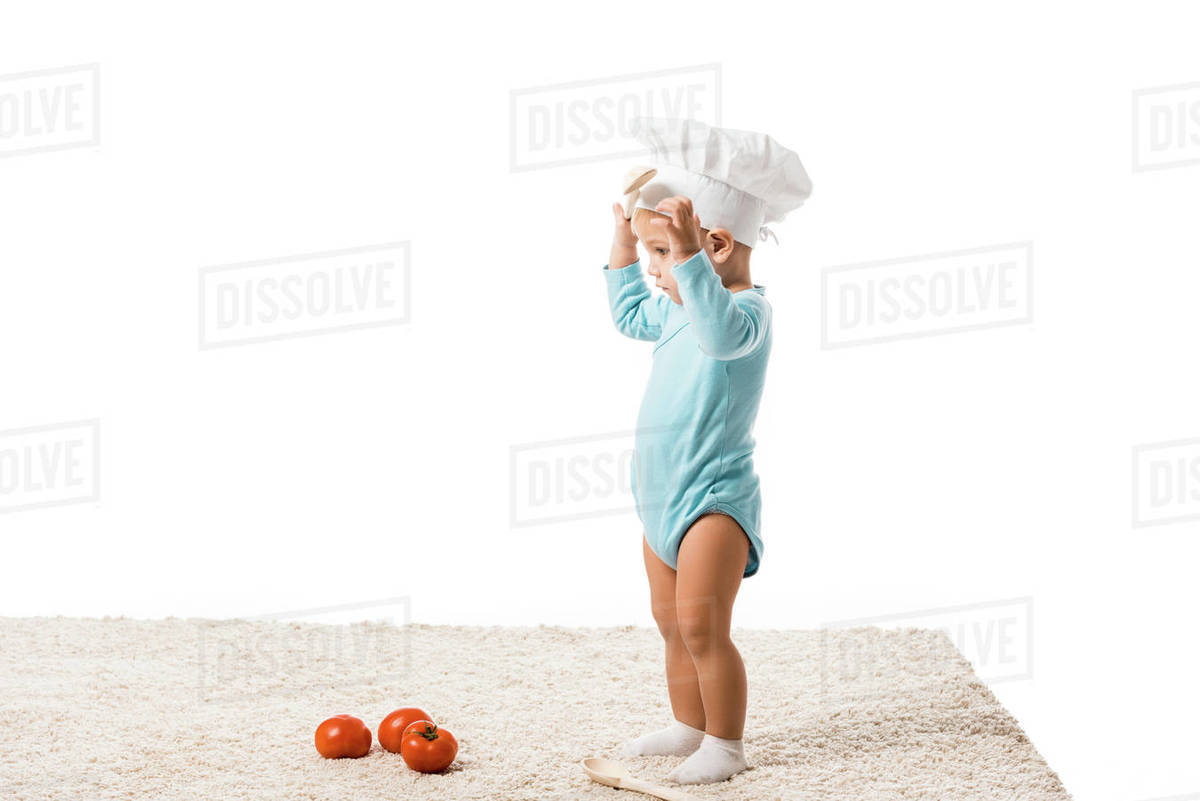 Toddler boy in chefs hat standing near fresh tomatoes on carpet ...