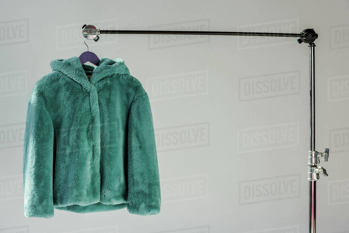 fluffy green faux fur coat hanging on rack at grey background with ...