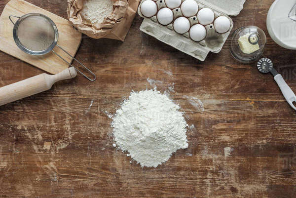 top view of white flour pile and baking ingredients on wooden table ...