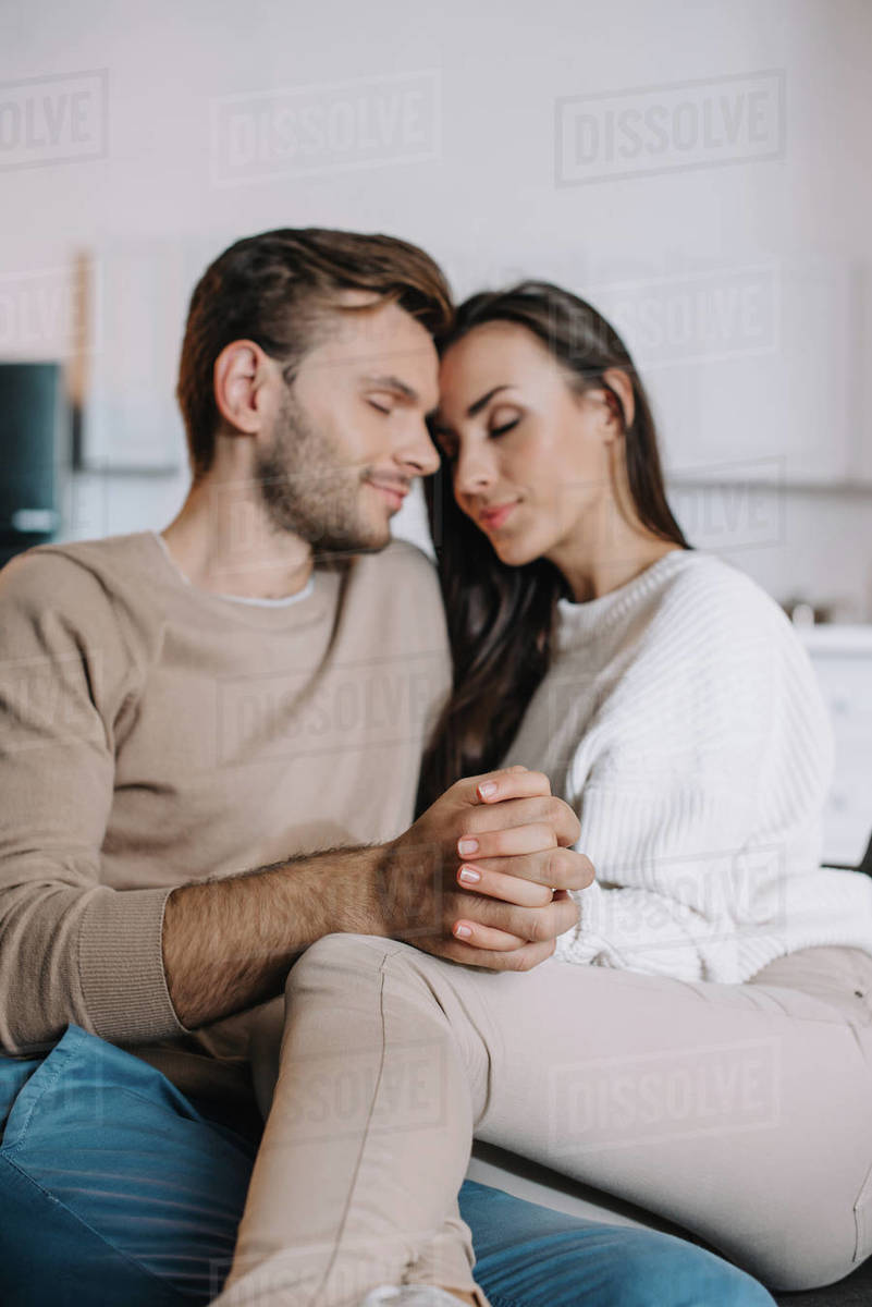 Happy young couple cuddling and holding hands on couch at home ...