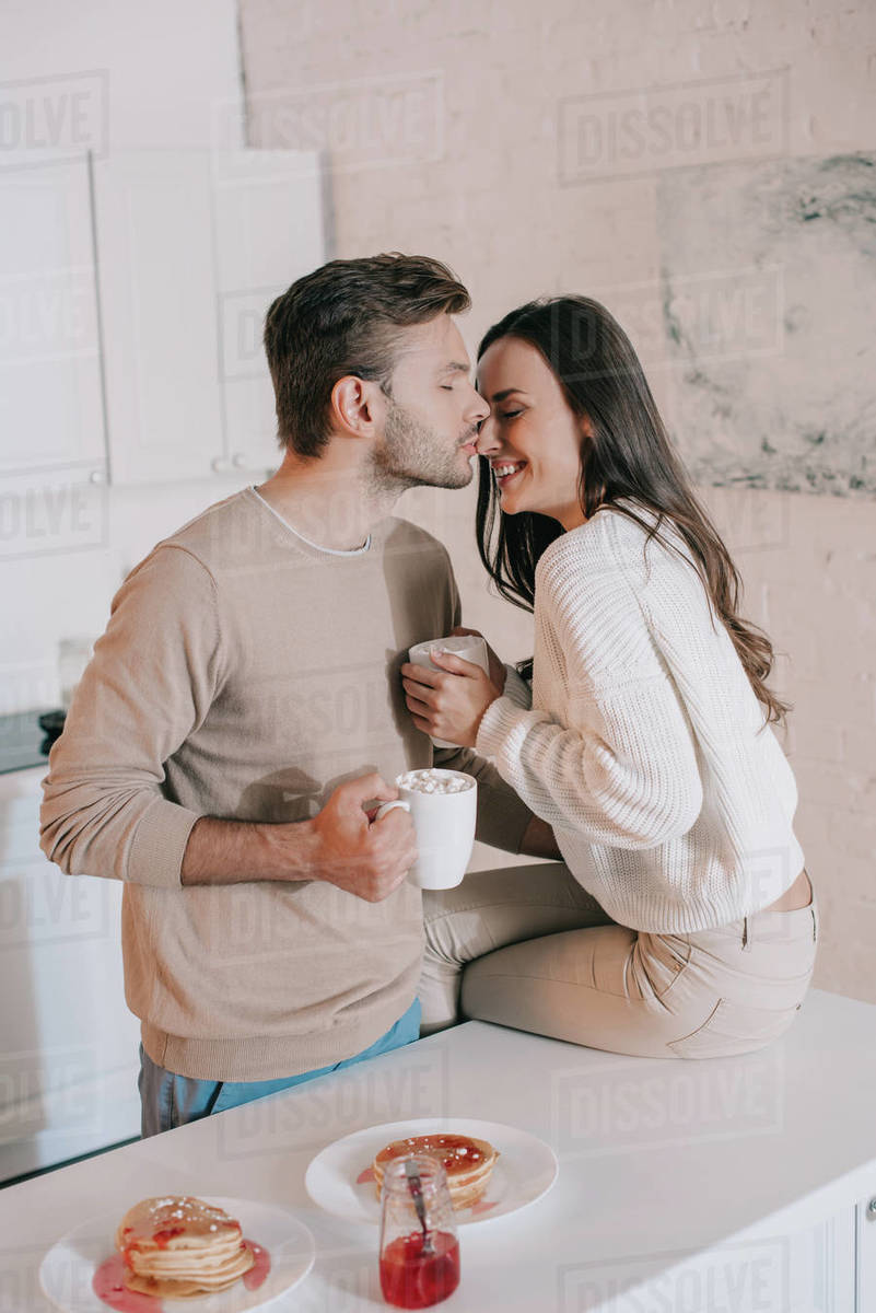 Beautiful young couple with cocoa and pancakes cuddling on kitchen ...
