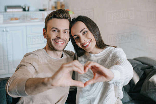 Beautiful young couple making heart symbol with hands and looking at ...