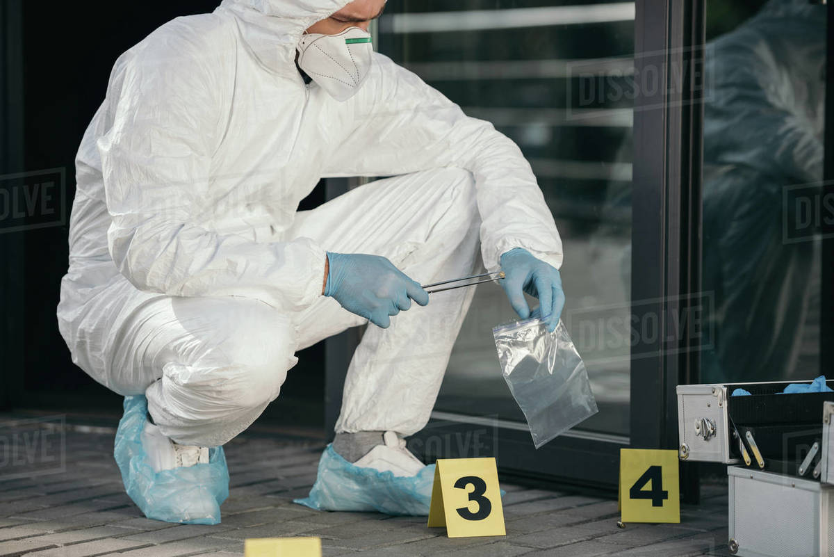 Male criminologist in protective suit and latex gloves packing evidence ...