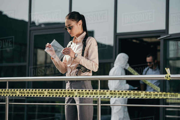 Female detective standing and looking at evidence in package - Royalty ...