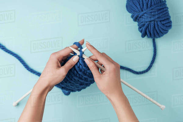 cropped shot of woman knitting on blue background with blue yarn ...
