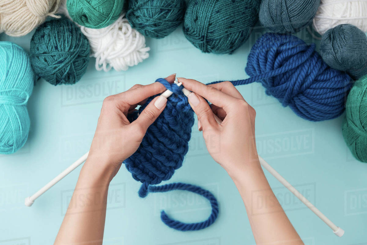 cropped shot of woman knitting on blue background with blue, green and ...