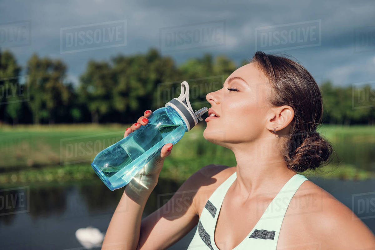 Side view of woman with eyes closed drinking water from bottle ...