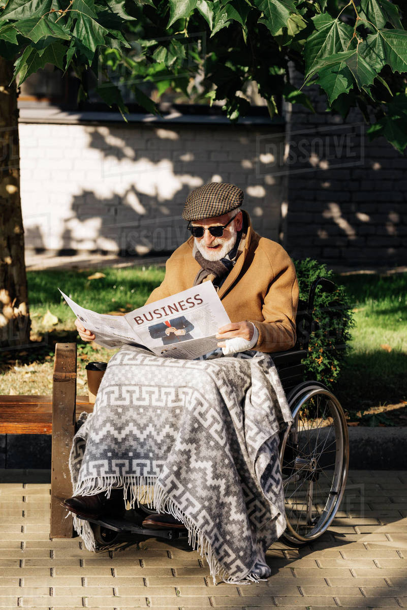 Elderly disabled man in wheelchair reading business newspaper on street ...