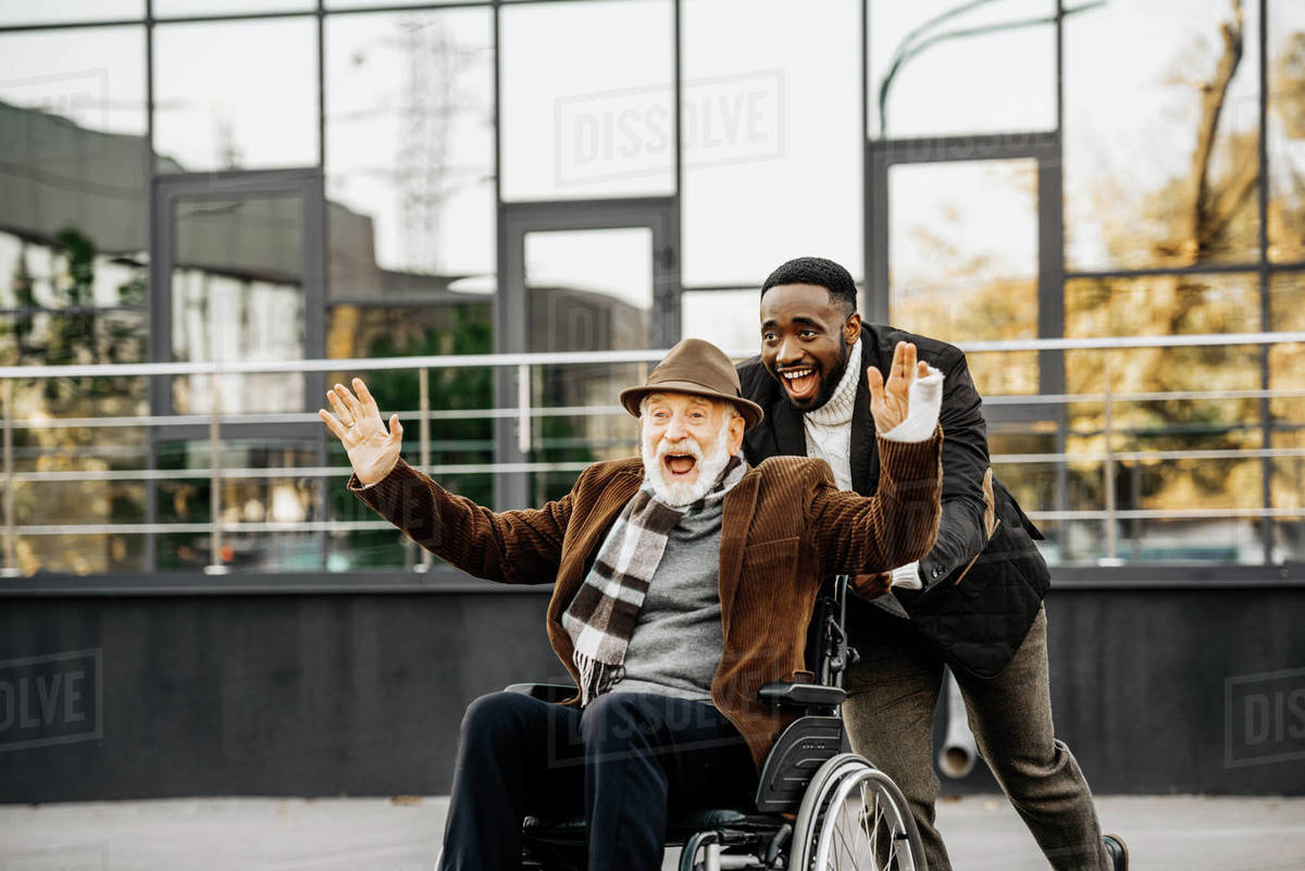 Happy senior disabled man in wheelchair and African American man having ...