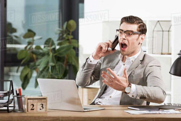 angry businessman talking by phone and screaming at workplace in office ...