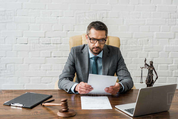 Serious male judge working with papers and laptop in office - Royalty ...