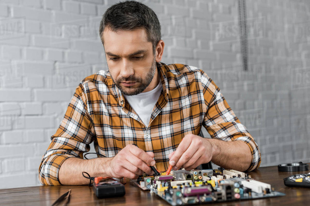 Concentrated computer engineer with tester examining motherboard ...