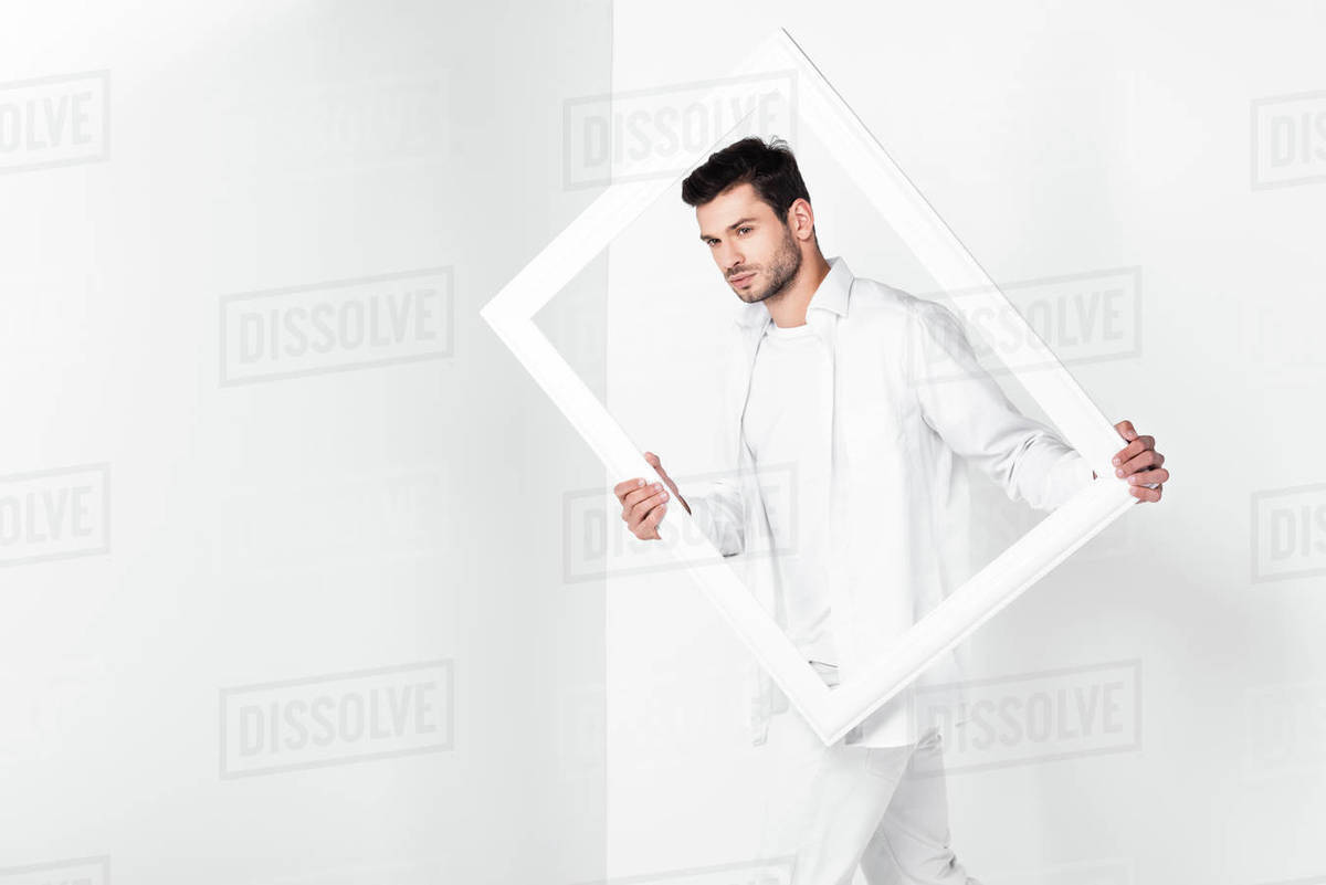 handsome adult man in total white holding frame - Stock Photo - Dissolve