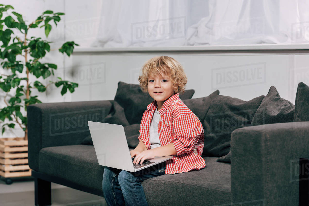 Little child looking at camera and using laptop on sofa at home - Stock ...