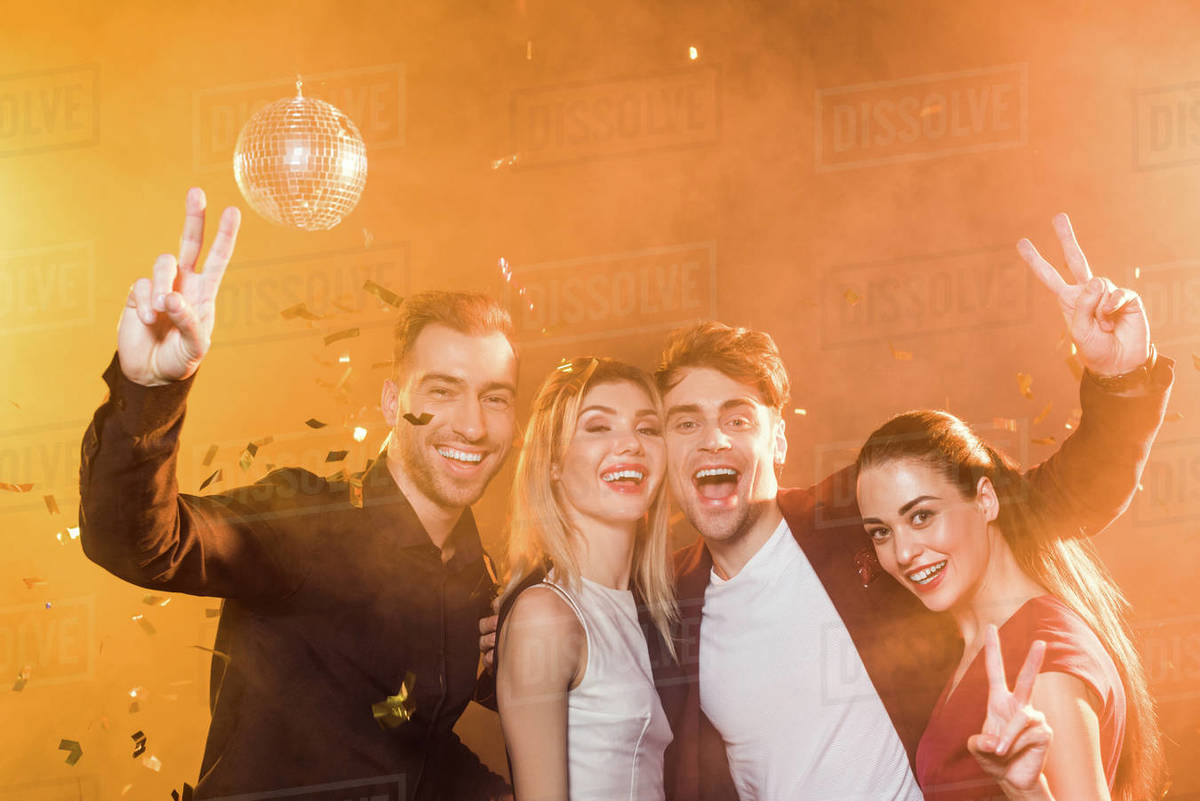 Group of smiling friends looking at camera and showing peace gesture ...
