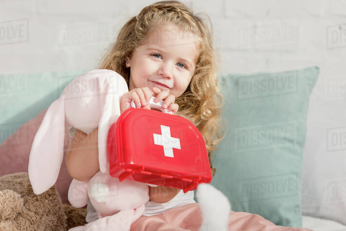 Adorable kid holding first aid kit and rabbit toy in children room ...
